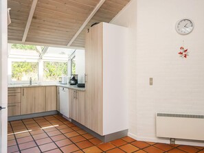 Uma cozinha com armários de madeira, um relógio de parede branco, uma janela e um radiador.