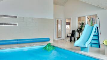 Piscina interna com escorregador, um banco e uma cadeira.