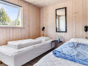 Quarto com duas camas, janela, espelho e uma mesinha.