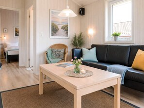 Uma sala de estar moderna com uma mesa de centro de madeira, um sofá de couro preto, uma poltrona de vime e um quadro pendurado na parede.