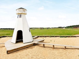 Um farol sobre uma plataforma de madeira, com um campo gramado e edifícios ao fundo.