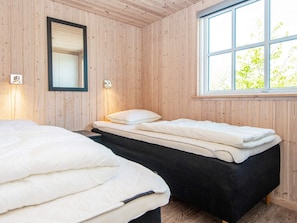 Quarto com duas camas, janela com vista para vegetação e espelho fixado na parede.
