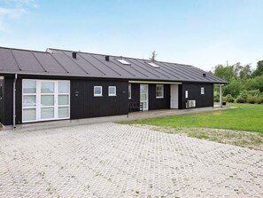 Um edifício preto com teto plano, uma grande porta de garagem e entrada pavimentada.