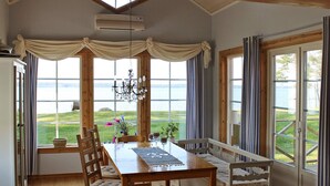 Uma sala de jantar com mesa e cadeiras de madeira, um candelabro e grandes janelas com cortinas.
