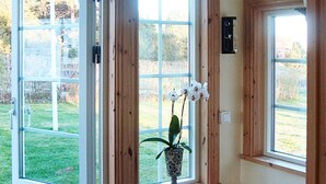 Quarto com uma janela grande, uma orquídea em vaso e vista para uma área gramada.