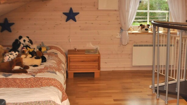 Um quarto aconchegante com piso de madeira, cama com colcha florida, mesa de cabeceira com abajur e janela com cortinas.
