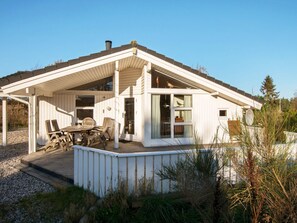 Uma casa térrea com varanda coberta, área de refeições com cadeiras e vista para a paisagem ao redor.