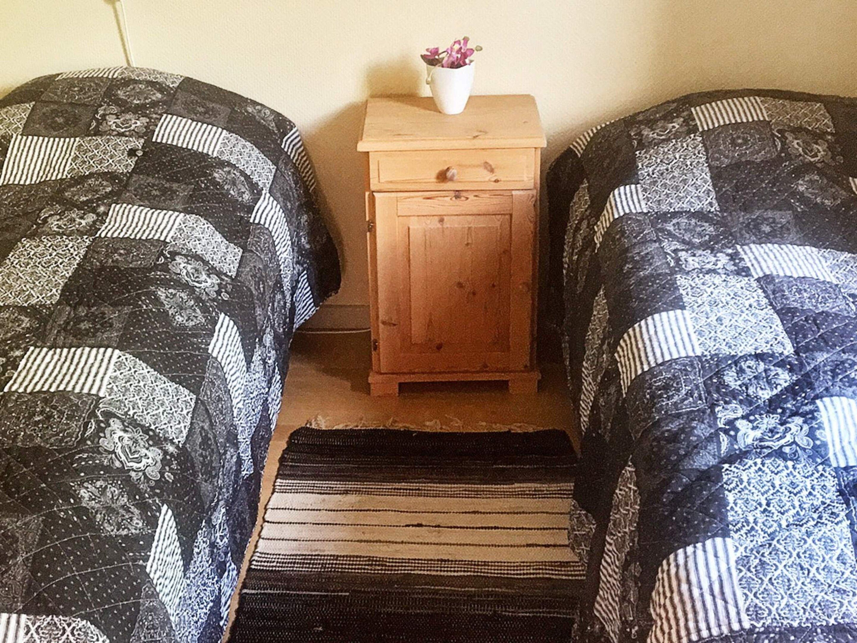 Quarto com duas camas, cada uma com colcha estampada, um criado-mudo de madeira e um vaso de flores, e um tapete listrado.