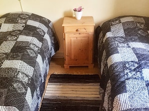 Quarto com duas camas, cada uma com colcha estampada, um criado-mudo de madeira e um vaso de flores, e um tapete listrado.