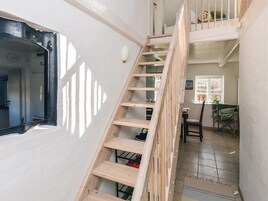Escadaria de madeira em vários níveis, com corrimão, que leva a um quarto com janela e cadeira.