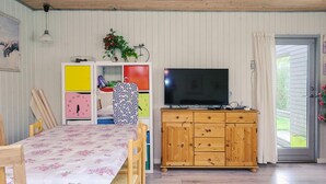 Um quarto com uma mesa de jantar de madeira, cadeiras, uma televisão em um móvel de madeira e uma janela com cortinas.