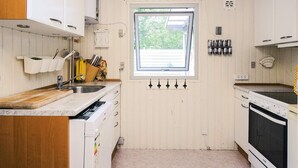 Uma cozinha compacta com armários brancos, forno embutido e janela que traz luz natural.
