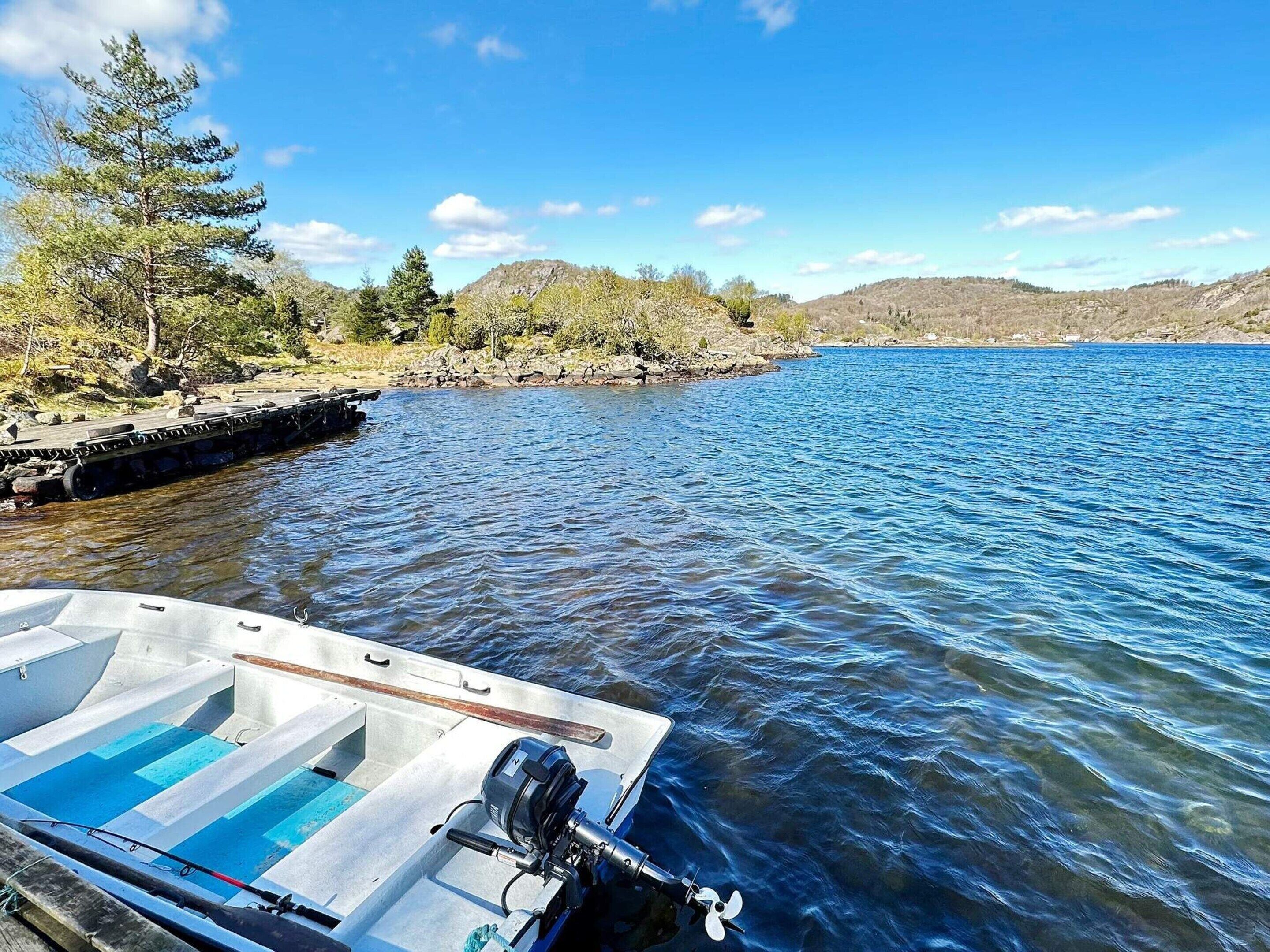 Um barco em um lago calmo, com um cais à esquerda e árvores ao fundo.