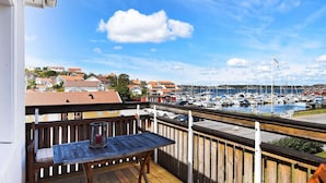 Um deck de madeira com mesa e cadeiras, com vista para uma marina com barcos e casas ao fundo.