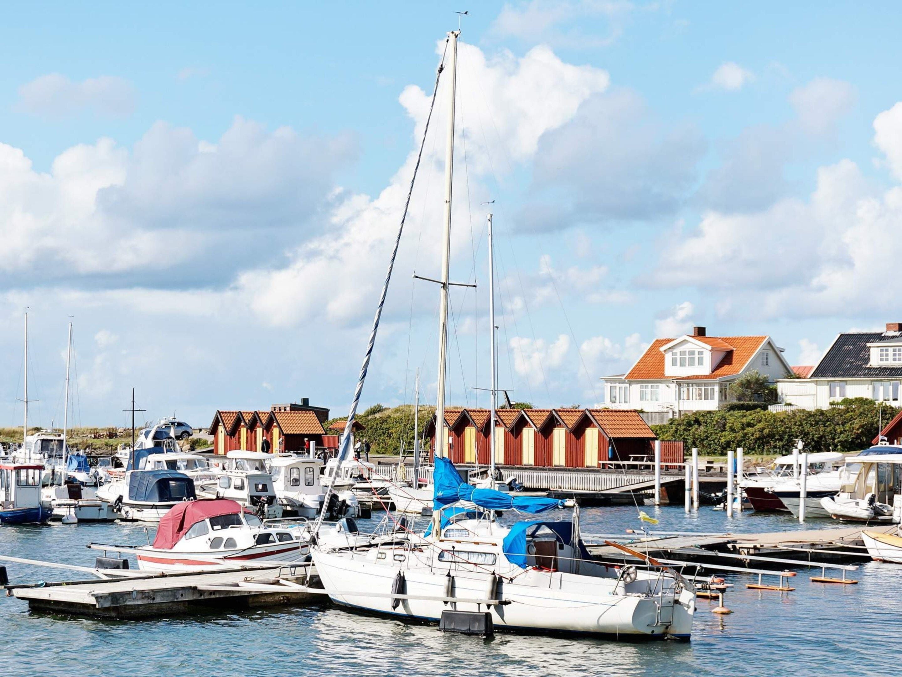 Uma marina com barcos atracados, uma fileira de casas com telhados vermelhos e um céu claro.