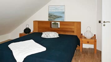 Quarto com cama, mesa de cabeceira, luminária, porta e quadro pendurado na parede.