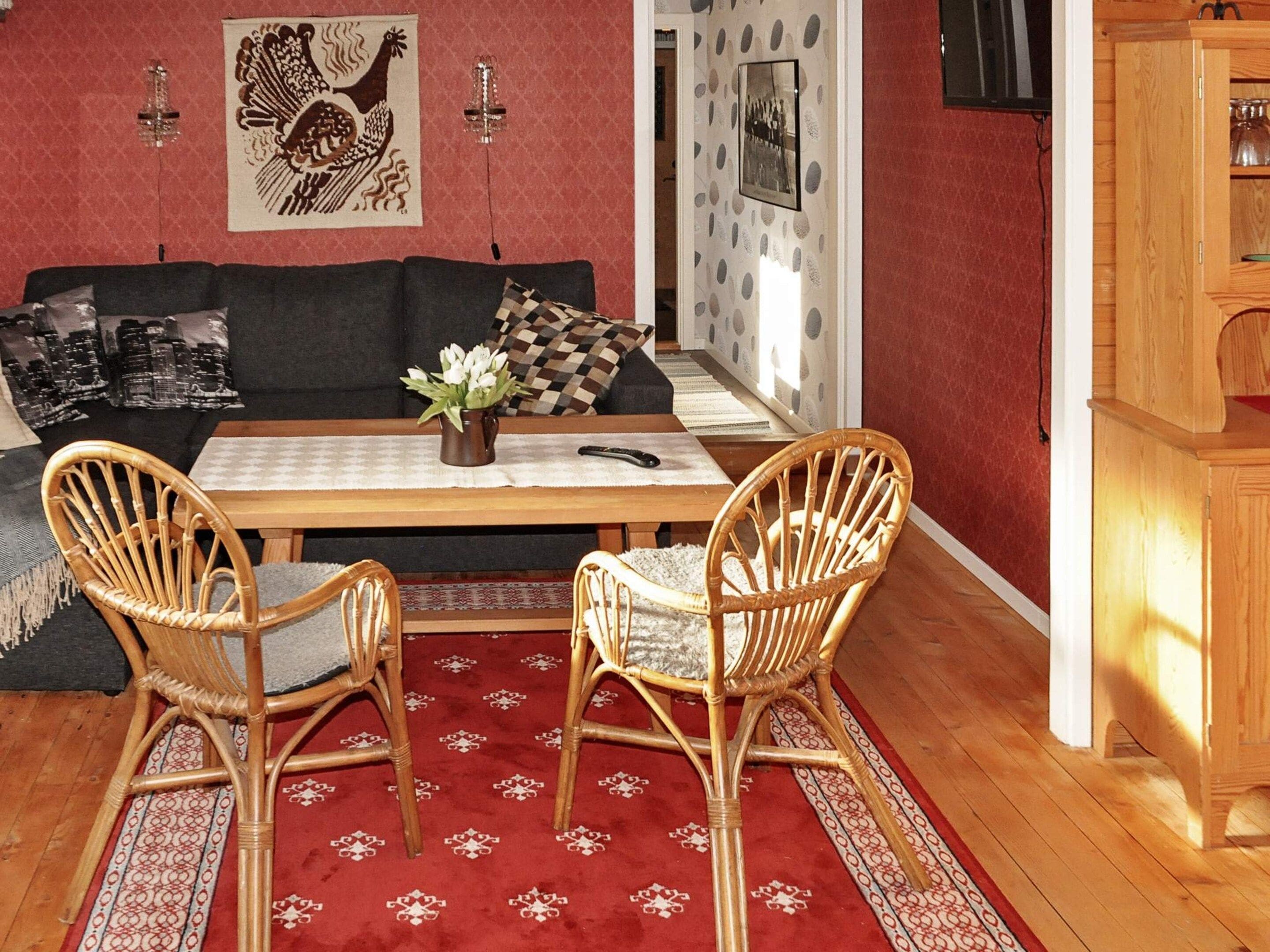 Sala de estar com sofá, duas poltronas, mesa, tapete estampado em vermelho e um armário de madeira.