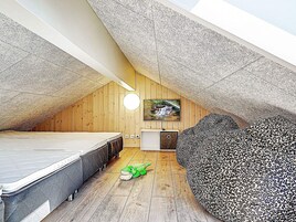 Um quarto de sótão acolhedor, com teto inclinado, uma cama, um pequeno penteoude e um banquinho estampado com padrão de leopardo, além de uma TV na parede.
