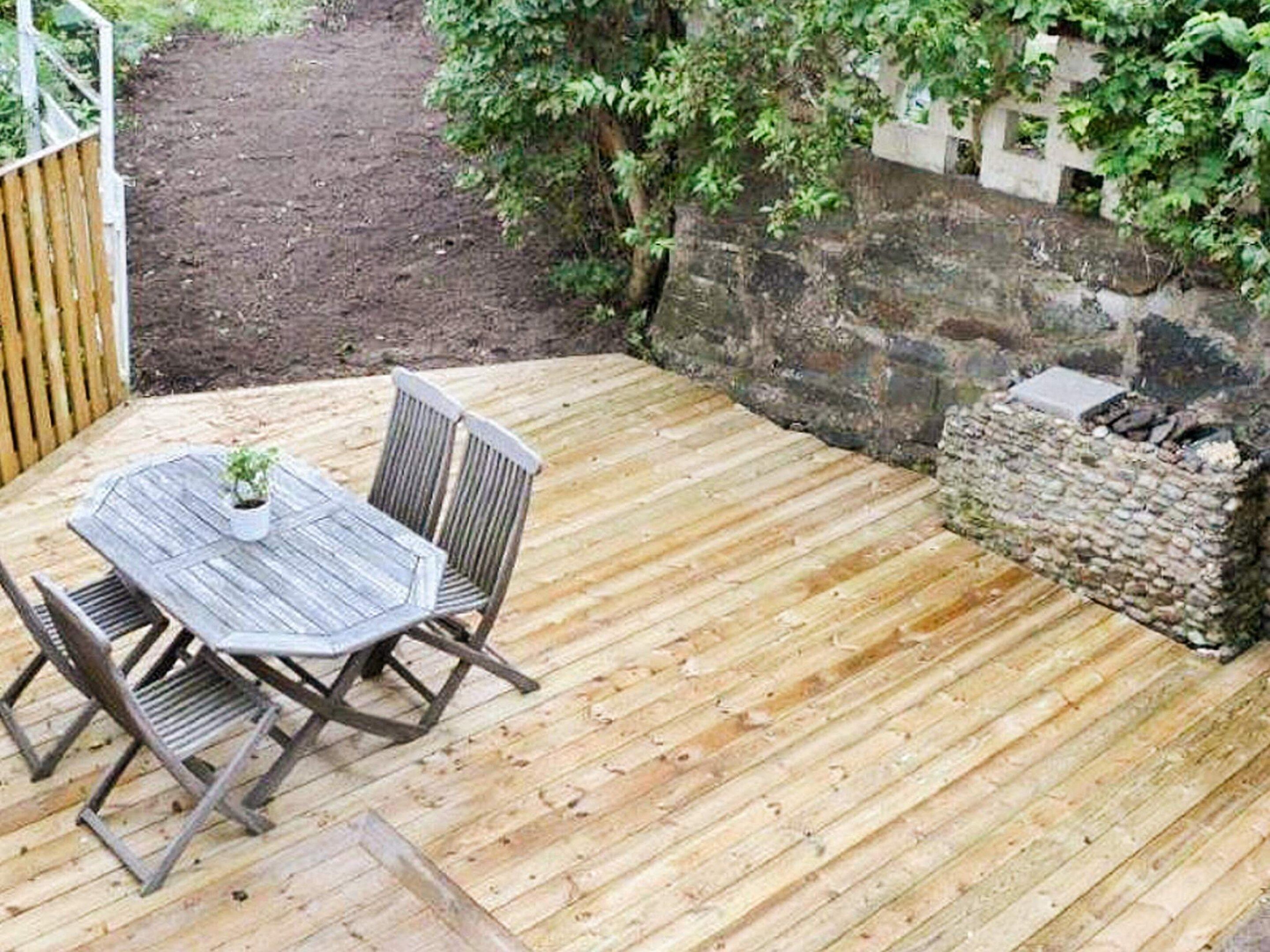 Um deck de madeira com uma mesa e cadeiras, cercado por um muro de pedra e uma cerca de madeira.