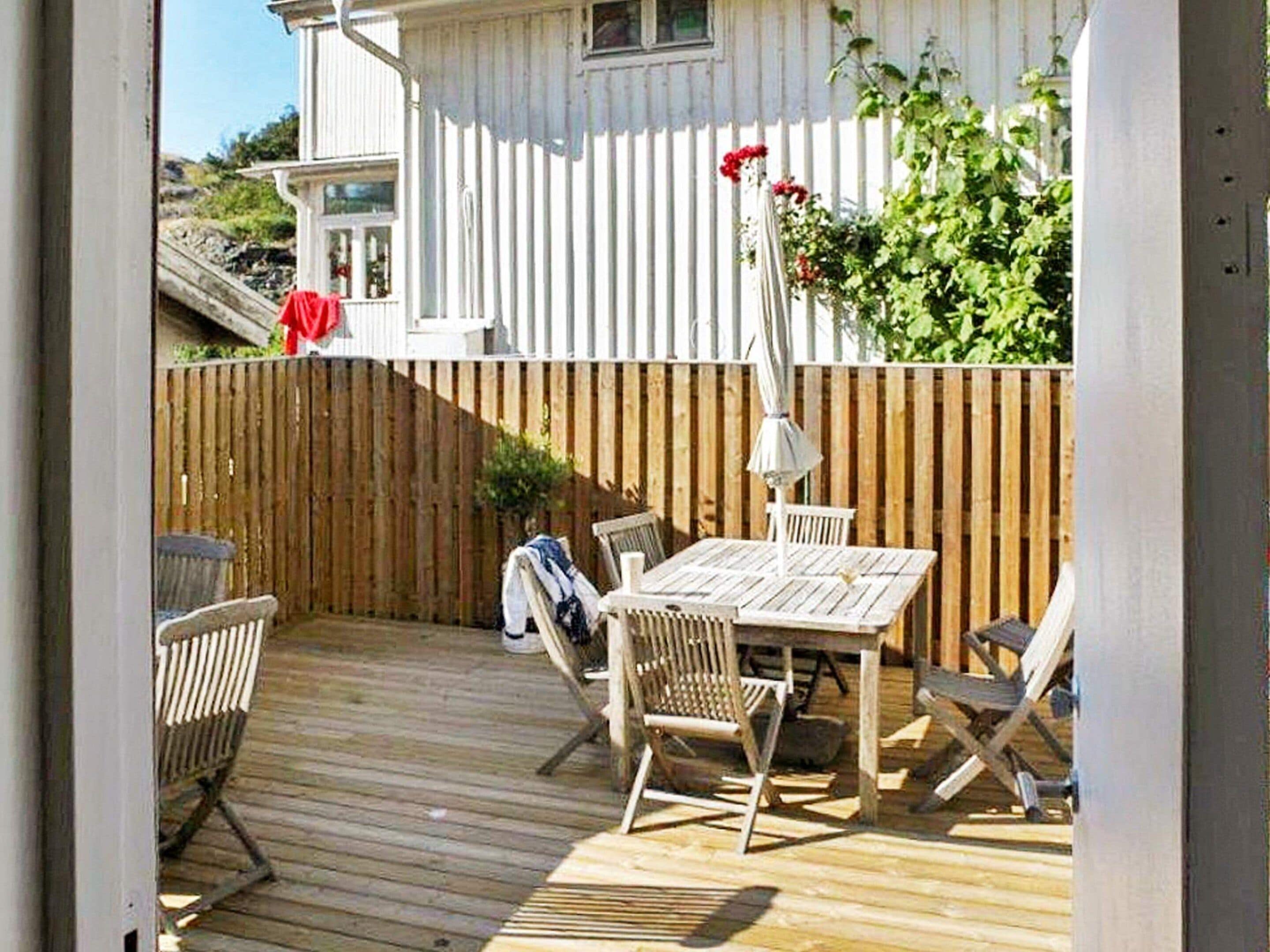 Um deck de madeira com mesa e cadeiras, uma cadeira suspensa e um vaso com planta.