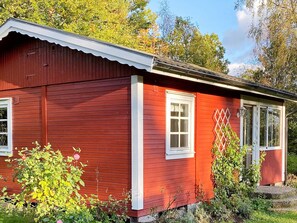Uma casa de madeira vermelha com moldura de janela branca, porta com moldura branca e pequena varanda.