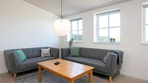 Uma sala de estar moderna com um sofá modular cinza, uma mesa de centro de madeira e um tapete com padrão geométrico.