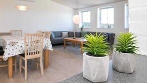 Uma sala de jantar com uma mesa posta para dois, um sofá e duas plantas em vasos.