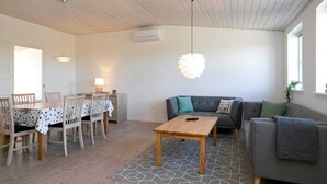 Sala de estar moderna com área de jantar, destacando teto de madeira, tapete geométrico e sofá cinza com almofada verde.