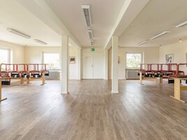 Um quarto espaçoso com piso de madeira, várias áreas de estar com cadeiras vermelhas e uma porta branca com sinal de saída.