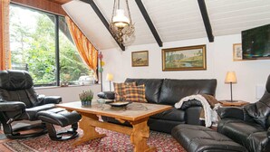 Uma sala de estar com mesa de centro de madeira, sofás de couro, tapete estampado e uma grande janela com cortinas.