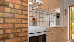 Uma cozinha com parede de tijolo, painel de azulejos brancos, eletrodomésticos de aço inoxidável e armários de madeira.