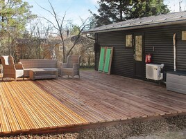 Um deck de madeira com mobiliário externo, um edifício com uma porta verde e um extintor de incêndio.