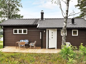 Uma cabana de madeira com telhado de telhas, um deck com cadeiras e uma porta.