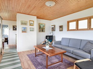 Uma sala de estar com teto de madeira, um sofá cinza, mesa de centro de madeira e tapete roxo.