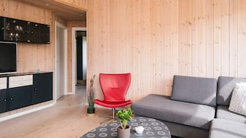 Uma sala de estar moderna com um sofá cinzento, uma poltrona vermelha e uma mesa de centro redonda com toalha de mesa estampada.