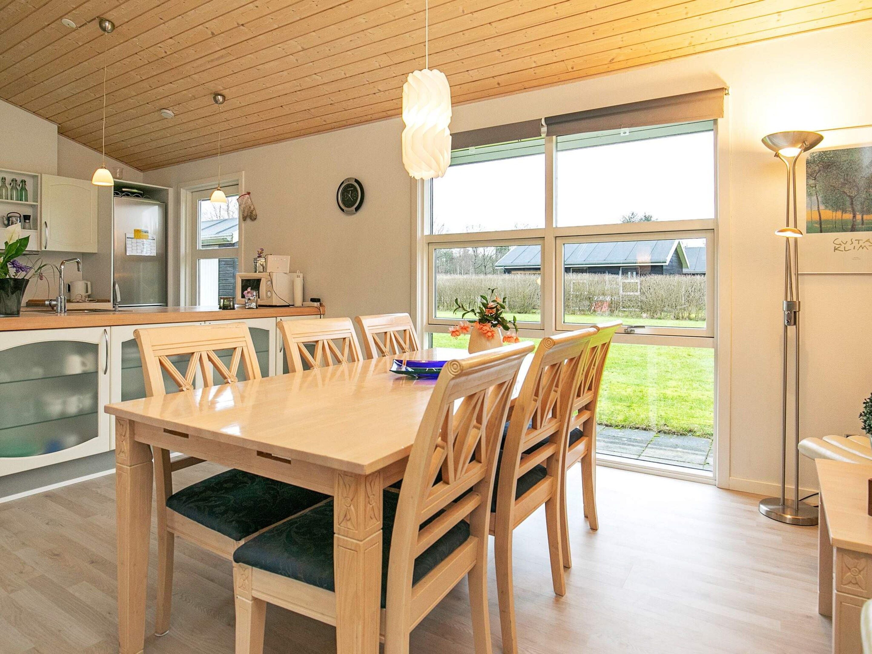 Cozinha moderna com armários de madeira, uma mesa de jantar com cadeiras e uma grande janela com vista para o exterior.
