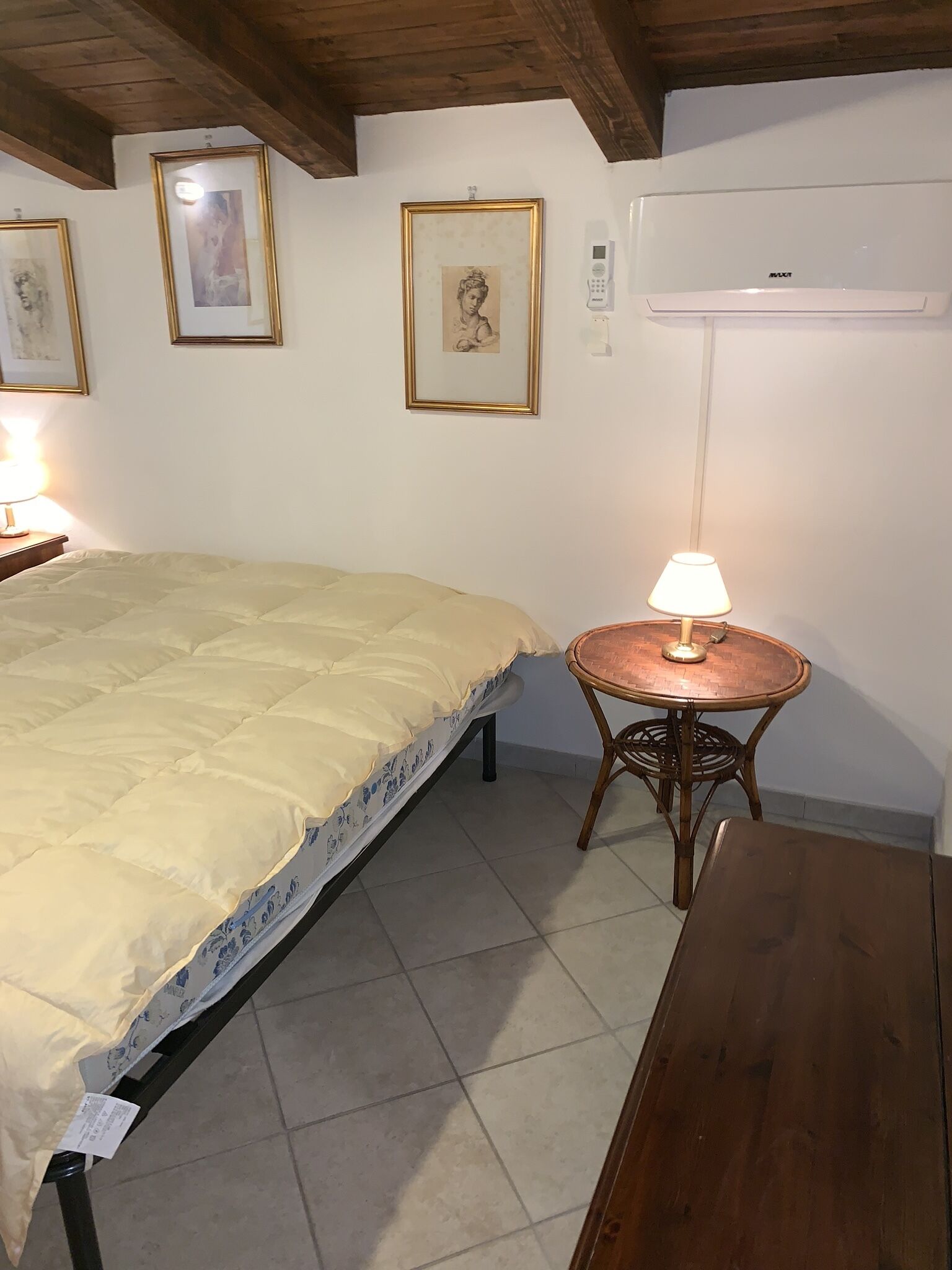 Quarto com cama, mesa de cabeceira com abajur, mesa de madeira e quadros na parede.