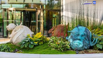 Jardim ajardinado com grandes esculturas e entrada do hotel Radisson.