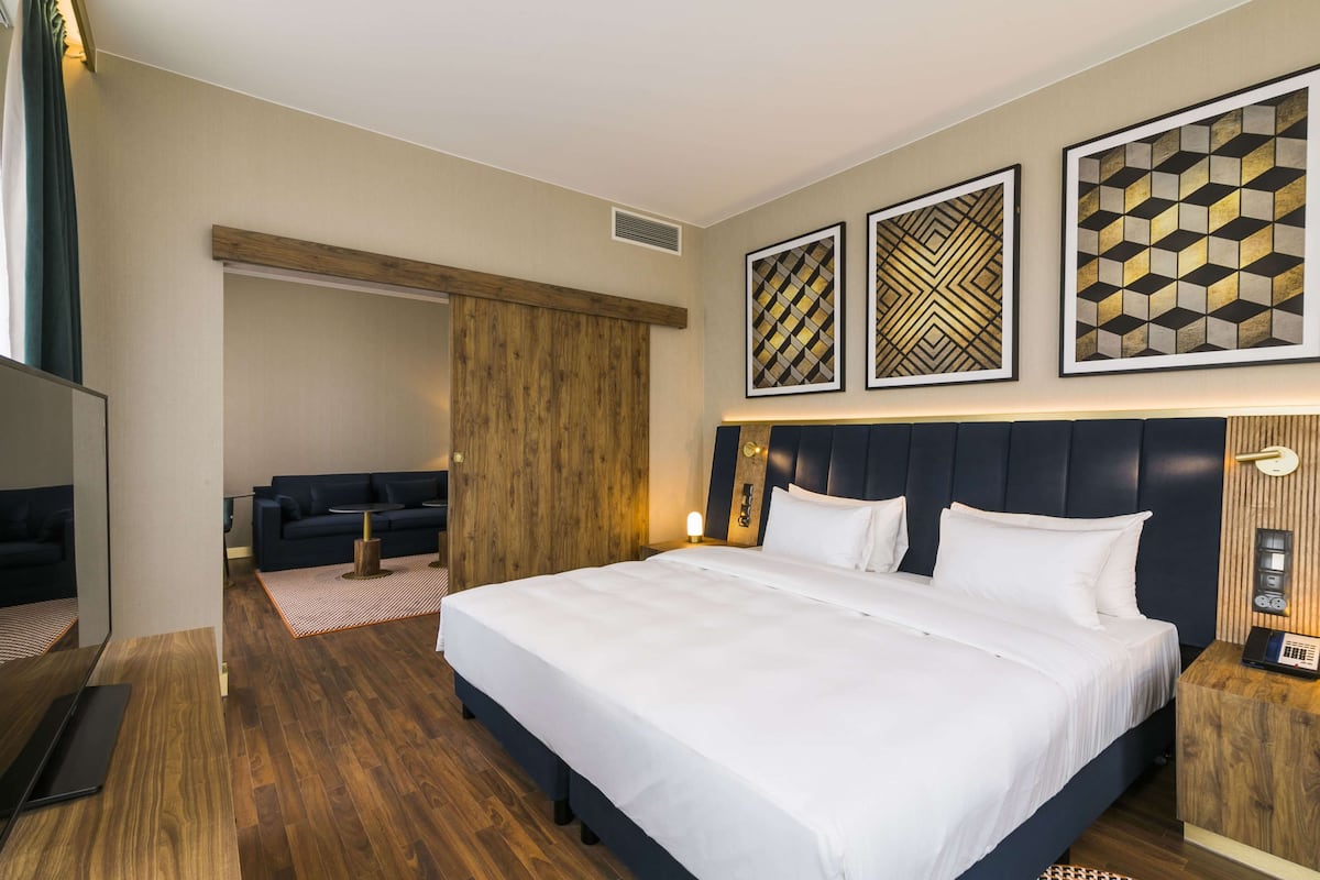Quarto de hotel moderno com uma cama grande, um sofá e uma TV. Três obras de arte emolduradas na parede.