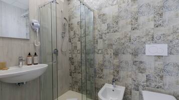 Uma casa de banho com chuveiro em cabine de vidro, lavatório, bidé e azulejos estampados.