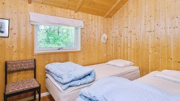 Quarto de cabana de madeira com duas camas, uma janela, uma cadeira e um ventilador.