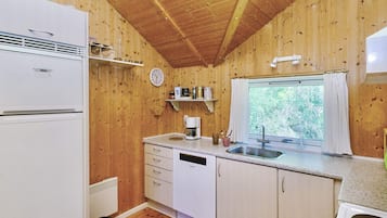 Cozinha compacta com paredes de madeira, uma geladeira branca, uma pia e uma janela com vista para o verde.