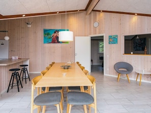 Uma sala de jantar moderna com uma mesa e cadeiras de madeira, um bar com banquetas e obras de arte nas paredes.