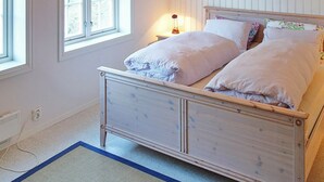 Quarto com cama de madeira, duas almofadas, mesa de cabeceira com abajur e janela com persianas.