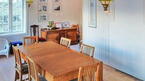 Uma sala de jantar com uma mesa e cadeiras de madeira, quadros nas paredes e duas lanternas penduradas.