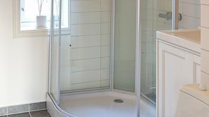 Um chuveiro no canto com porta de vidro, paredes azulejadas brancas e um armário branco.