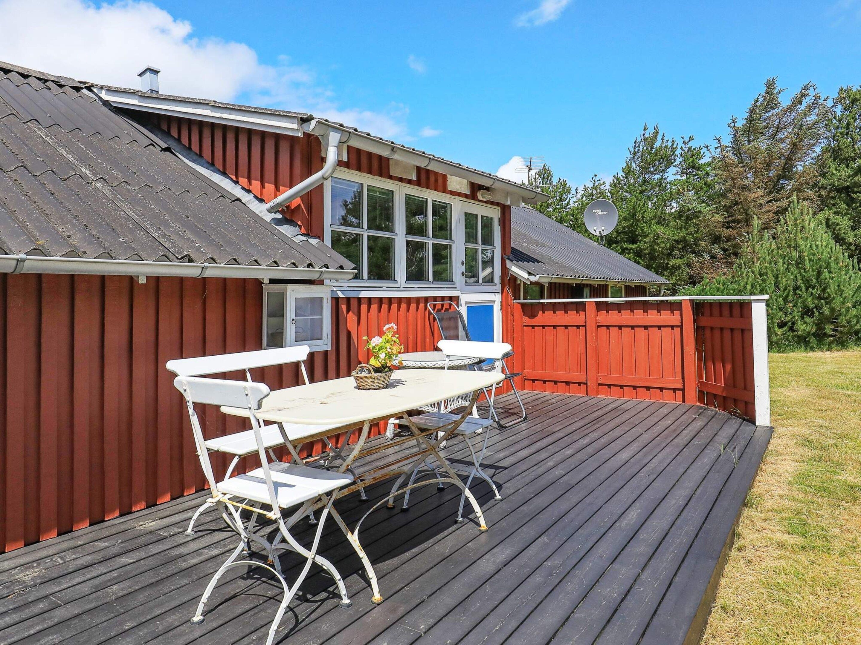 Um edifício vermelho com um terraço, uma mesa branca com cadeiras e uma porta azul.
