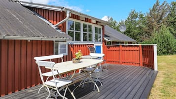 Um edifício vermelho com um terraço, uma mesa branca com cadeiras e uma porta azul.