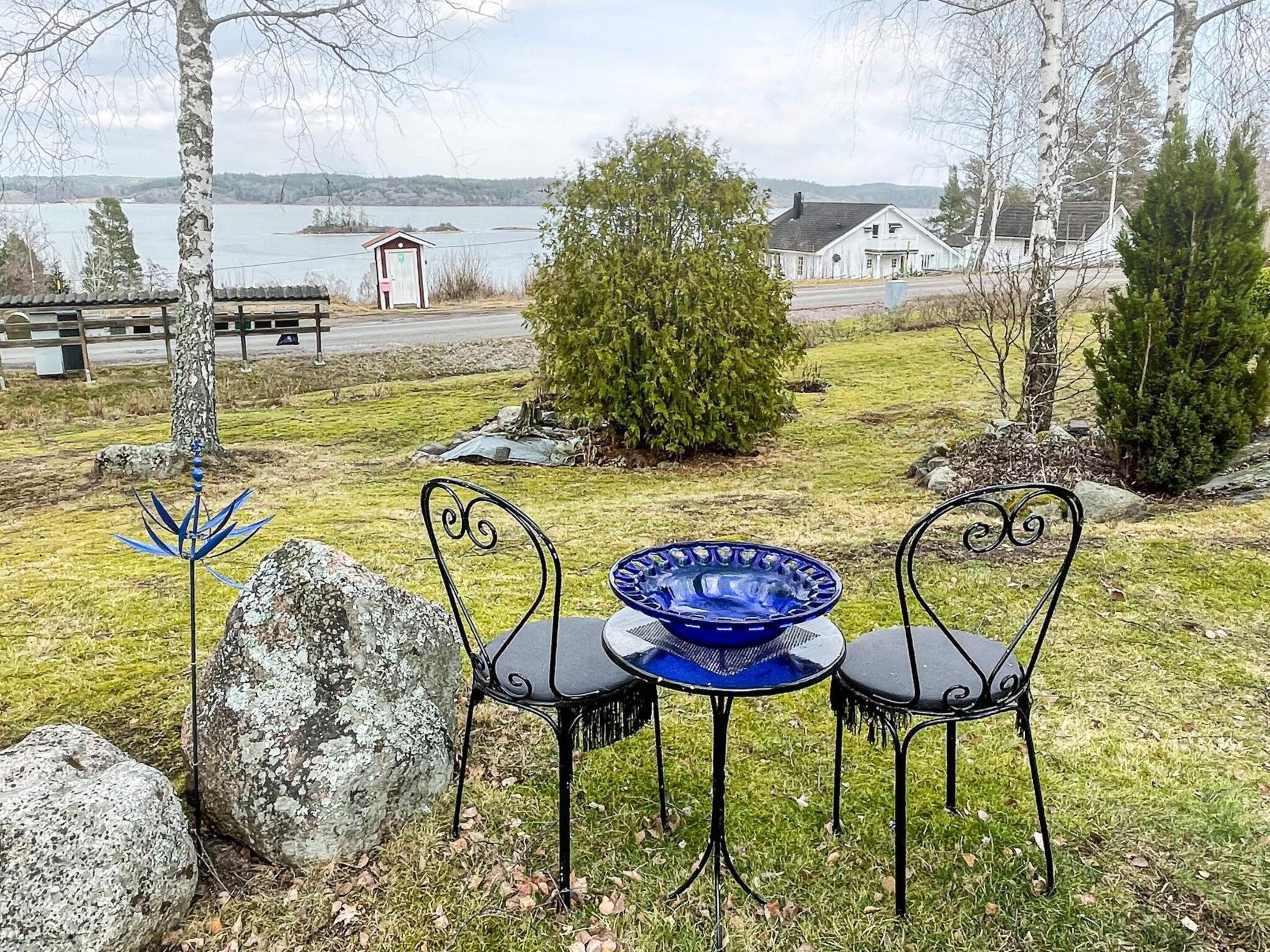 Mesa com cadeiras e uma tigela azul em área gramada com árvores e vista para um lago.