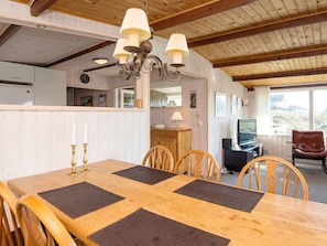 Uma área de refeições com mesa e cadeiras de madeira, um candelabro e uma televisão ao fundo.